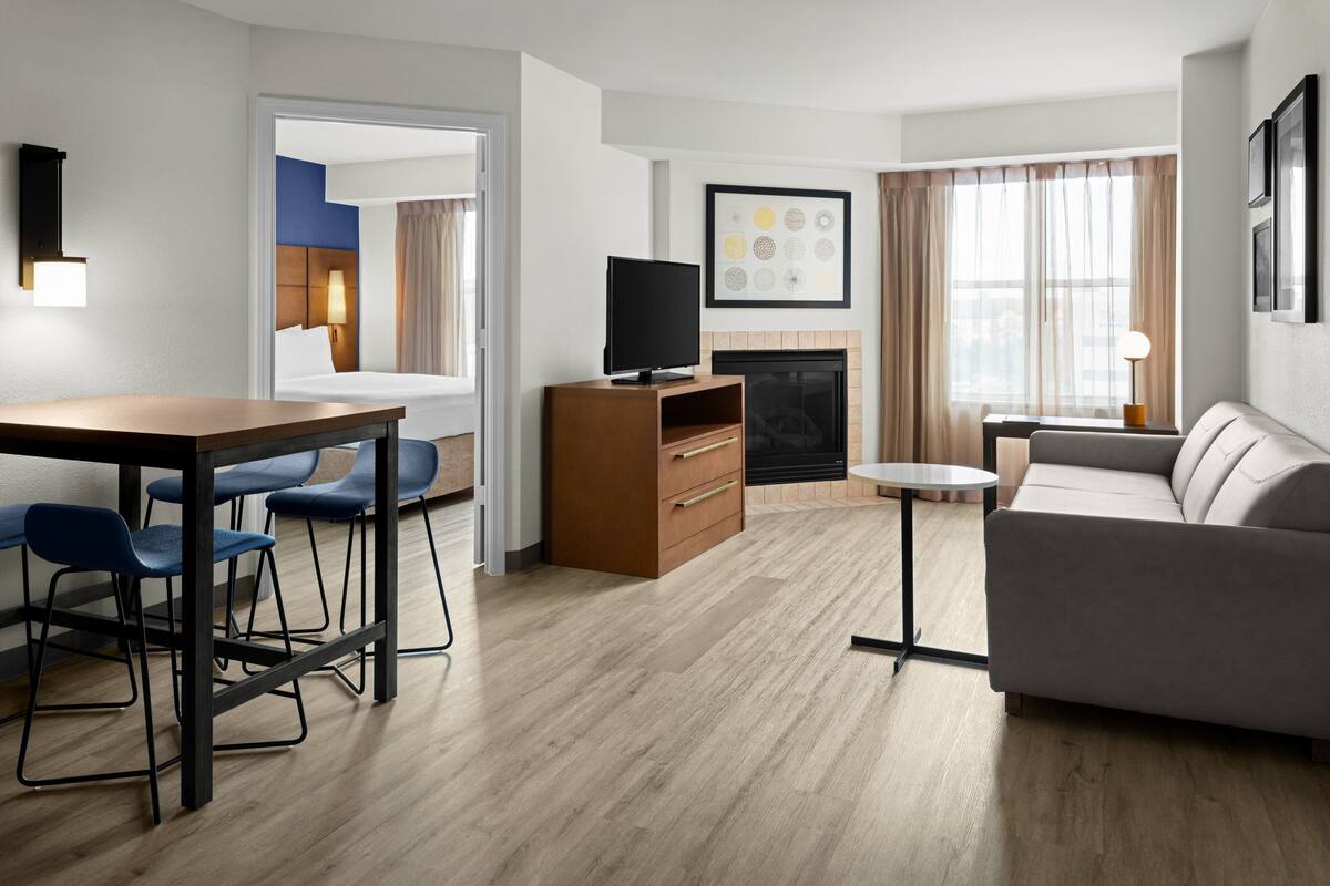 Quarto de hotel moderno com piso de madeira, sofá, televisão, lareira e área de jantar com cadeiras.