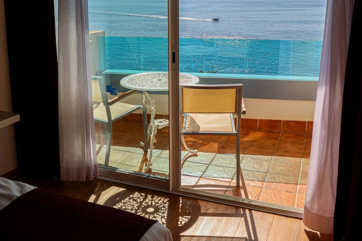 Quarto de hotel com varanda, uma cama e uma mesa com cadeiras.