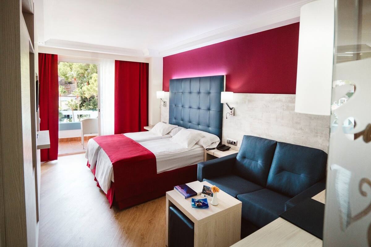 Quarto de hotel com cama, sofá, mesa de cabeceira e vista para o exterior.