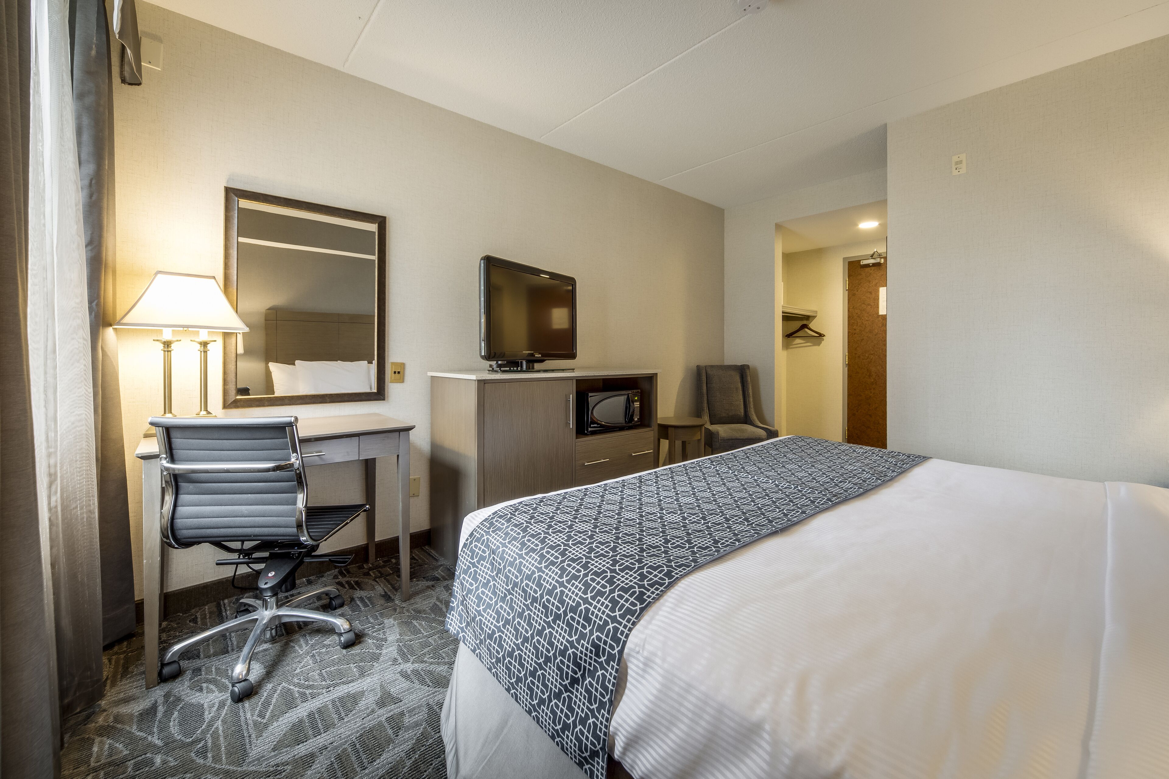 Quarto de hotel com cama, escrivaninha, cadeira e televisão.