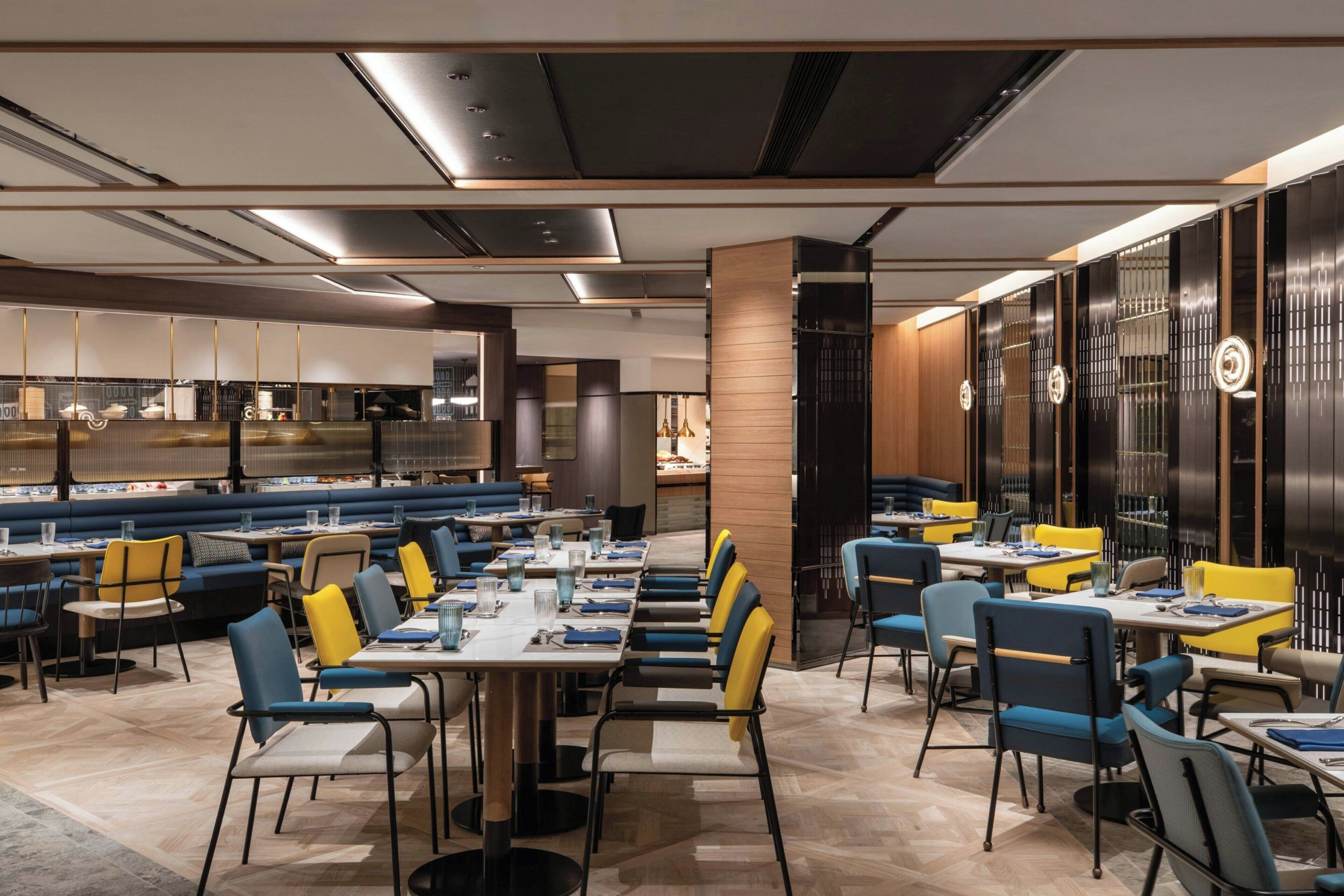 Restaurante moderno com uma mesa comunitária grande e cabines, com cadeiras em tons de azul e amarelo.
