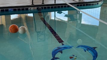 Piscina interna com um aro de basquete, um mural de golfinhos e vista para o exterior.