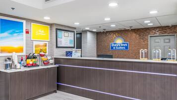 Uma área de recepção com a placa Day's Inn & Suites, um balcão com comodidades e uma parede de tijolos.
