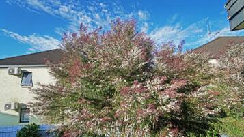 Um edifício residencial com telhado inclinado, aparelhos de ar condicionado e uma árvore com flores cor-de-rosa à frente.