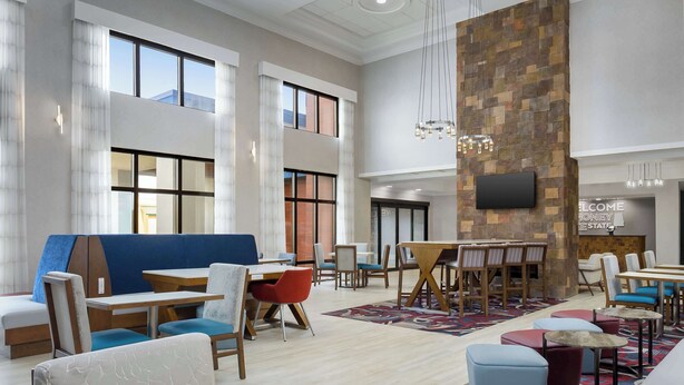 Um lobby de hotel moderno com áreas de estar, uma TV na parede e um letreiro com a frase 'Welcome Honey State'.