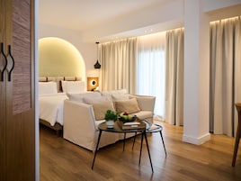Quarto de hotel moderno com cama, sofá, mesa redonda e cortinas.