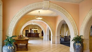 Um hall espaçoso com teto alto, grandes colunas em arco e área de estar central com mesa e cadeiras.