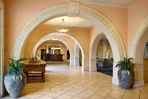 Um hall espaçoso com teto alto, grandes colunas em arco e área de estar central com mesa e cadeiras.
