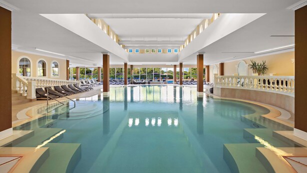 Uma grande piscina interior com espreguiçadeiras e vista para o exterior.