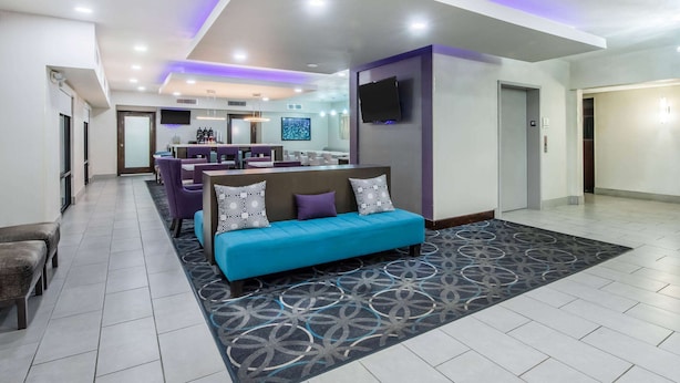 Um hall de hotel moderno com um sofá azul, cadeiras roxas e um tapete estampado.