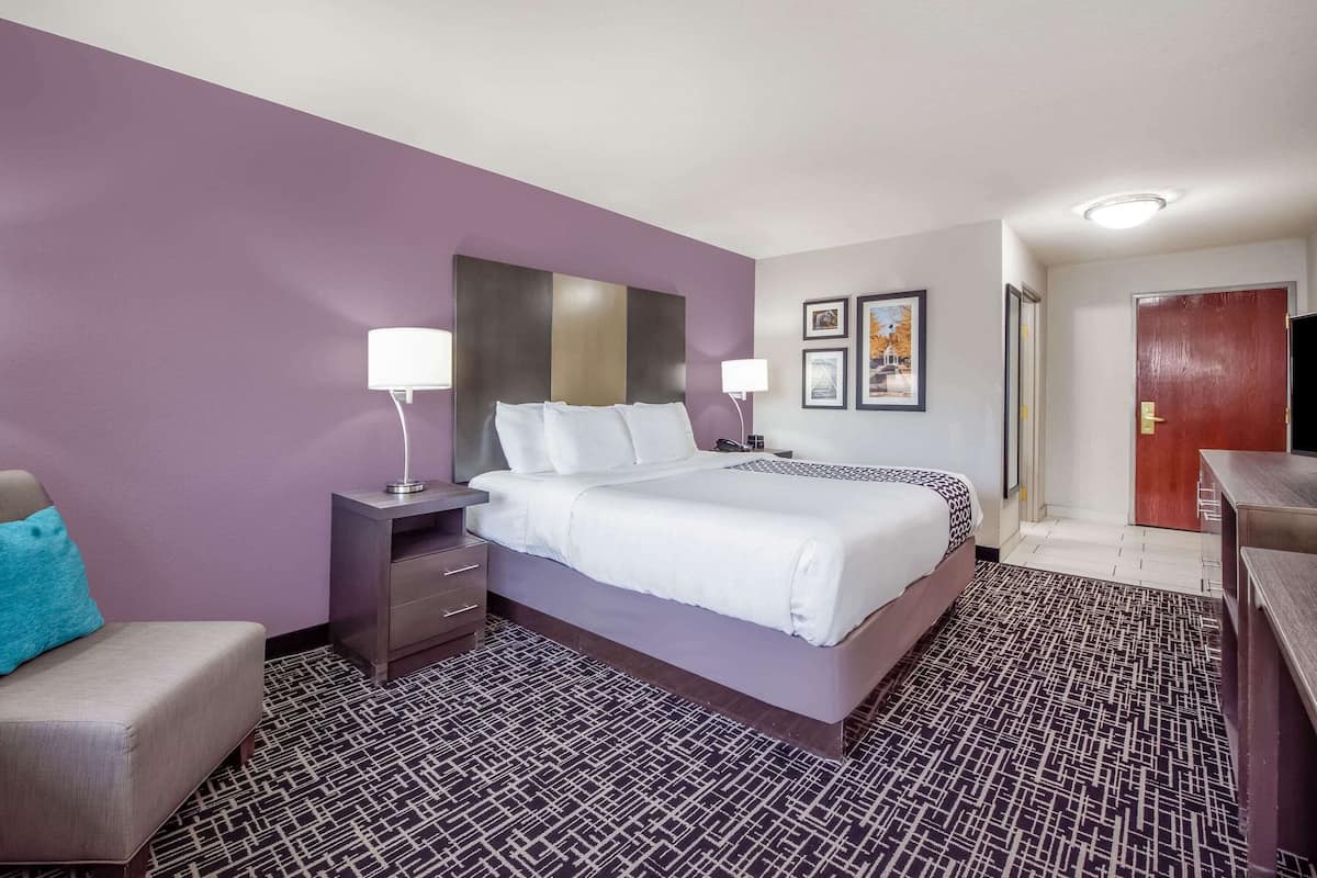 Quarto de hotel com uma cama grande, duas mesas de cabeceira, uma escrivaninha, uma cadeira e um tapete estampado.