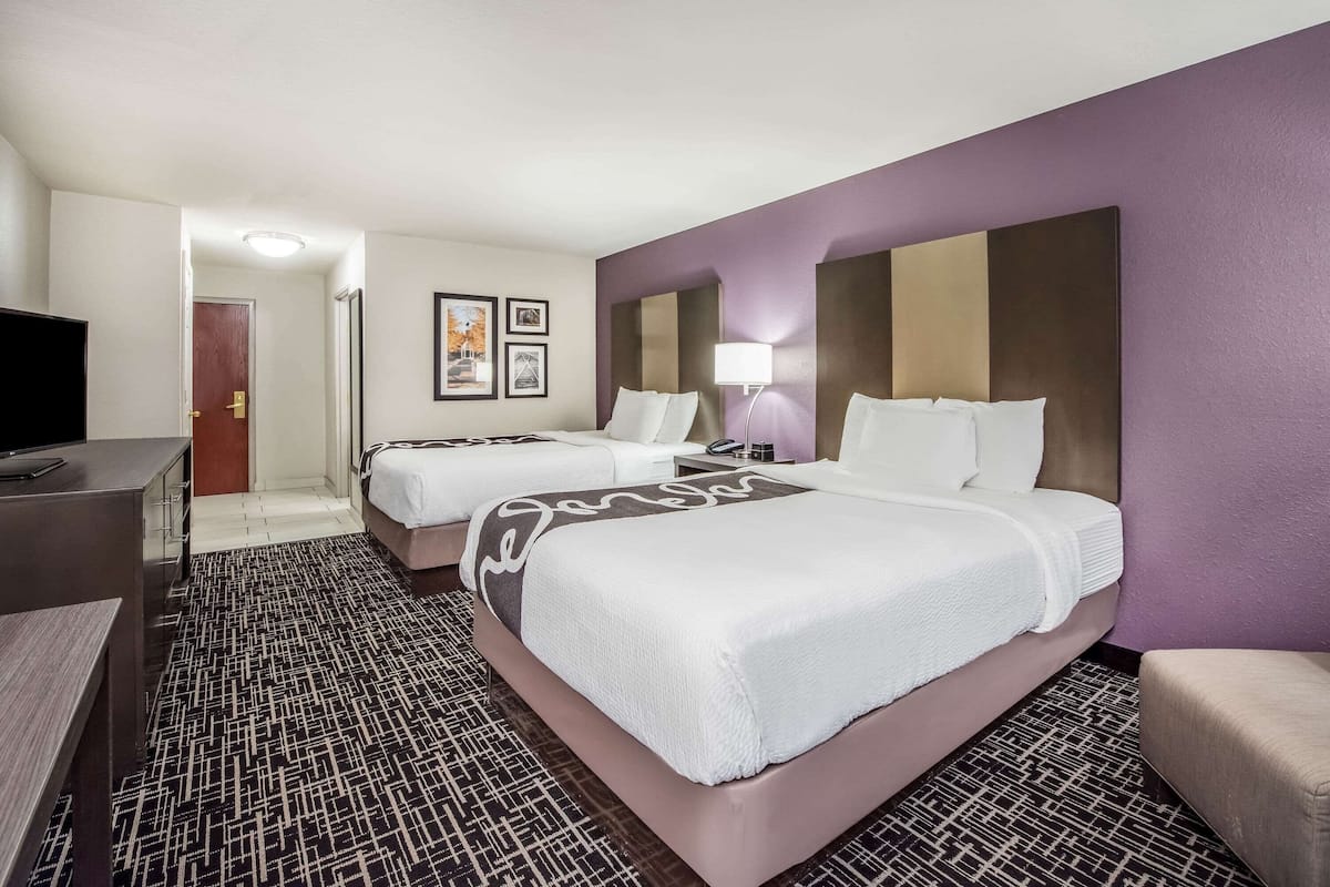 Quarto de hotel com duas camas, uma escrivaninha, televisão e um tapete estampado.
