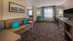 Quarto de hotel com sofá, escrivaninha, televisão e carpete estampado.