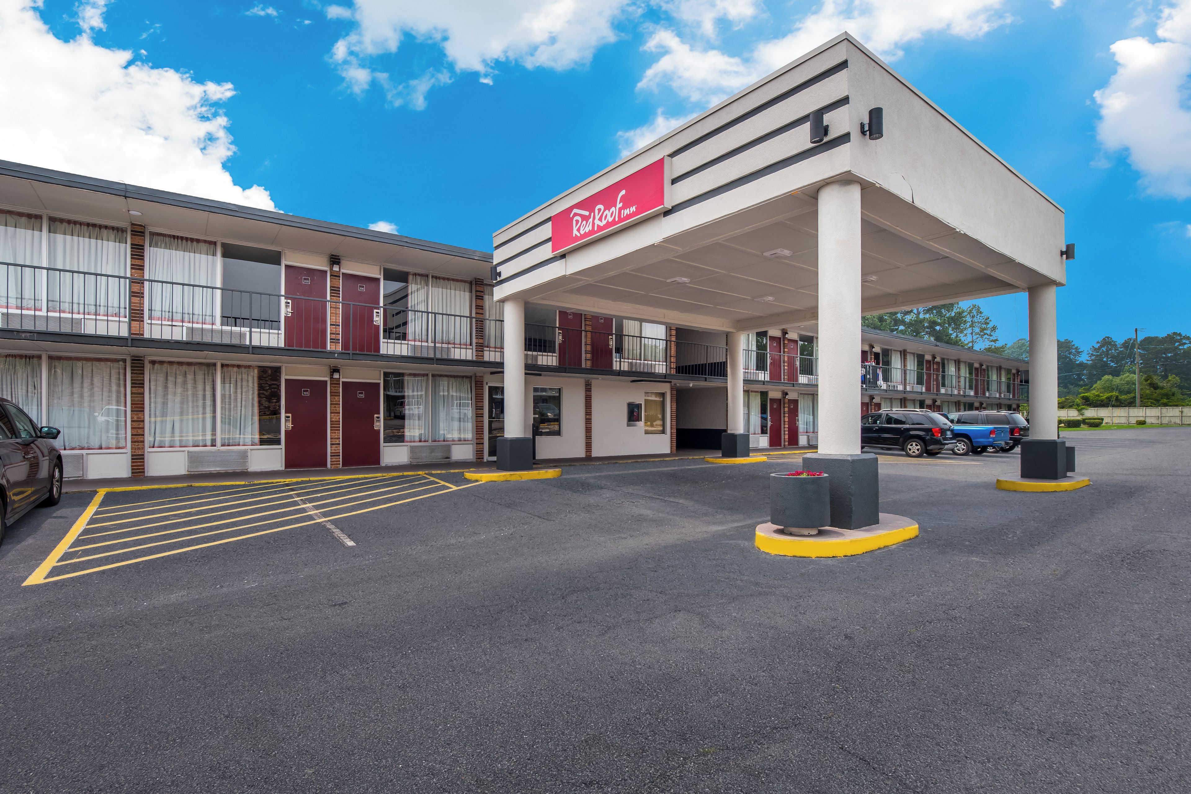 Red Roof Inn com área de estacionamento coberta e vários quartos com portas vermelhas.
