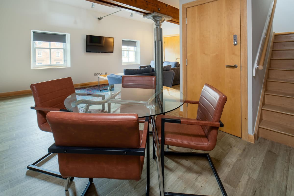 Sala de estar moderna com mesa de centro de vidro, poltronas de couro, TV fixada na parede e escada de madeira.