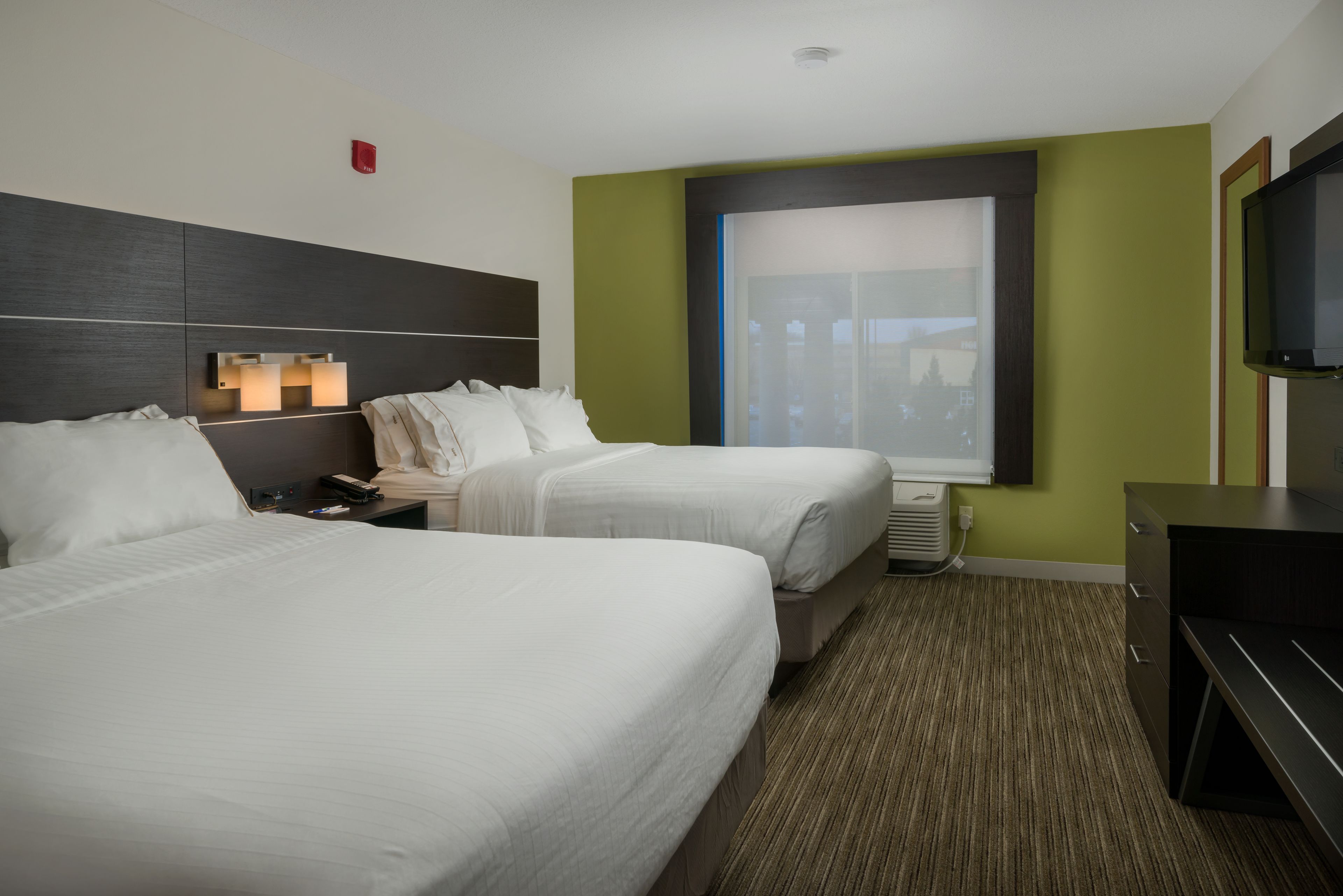 Quarto de hotel com duas camas, televisão, escrivaninha e janela com persianas.