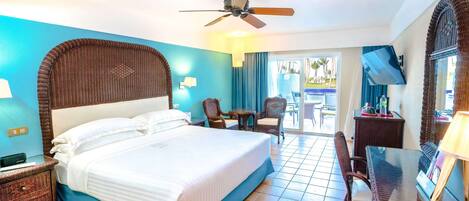 Quarto de hotel com uma cama grande, uma escrivaninha com cadeira, televisão e varanda com vista.