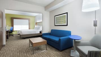 Quarto de hotel com cama, sofá azul, mesa pequena, cadeira, escrivaninha e abajur.