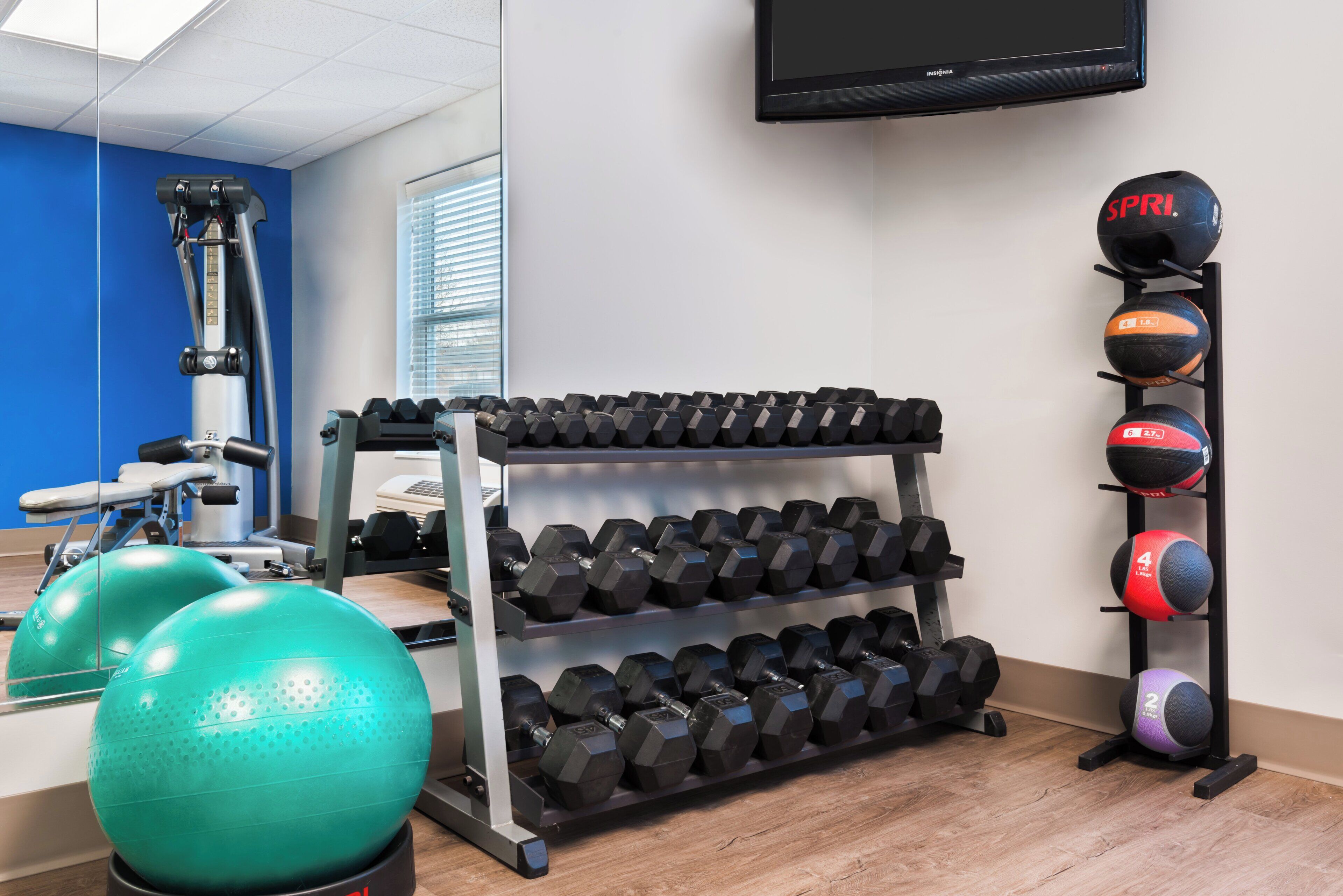 Academia com equipamentos de ginástica, incluindo halteres, um banco e uma bola de exercícios verde.