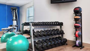 Academia com equipamentos de ginástica, incluindo halteres, um banco e uma bola de exercícios verde.