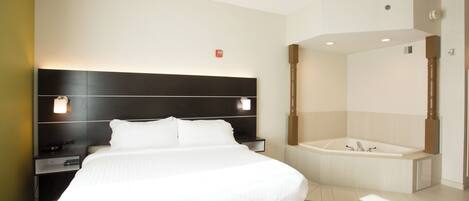 Quarto de hotel com uma cama grande, mesa de cabeceira, banheira integrada e um espelho.
