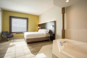 Quarto de hotel com cama, cadeira, janela grande, cabeceira, mesa de cabeceira e banheira.