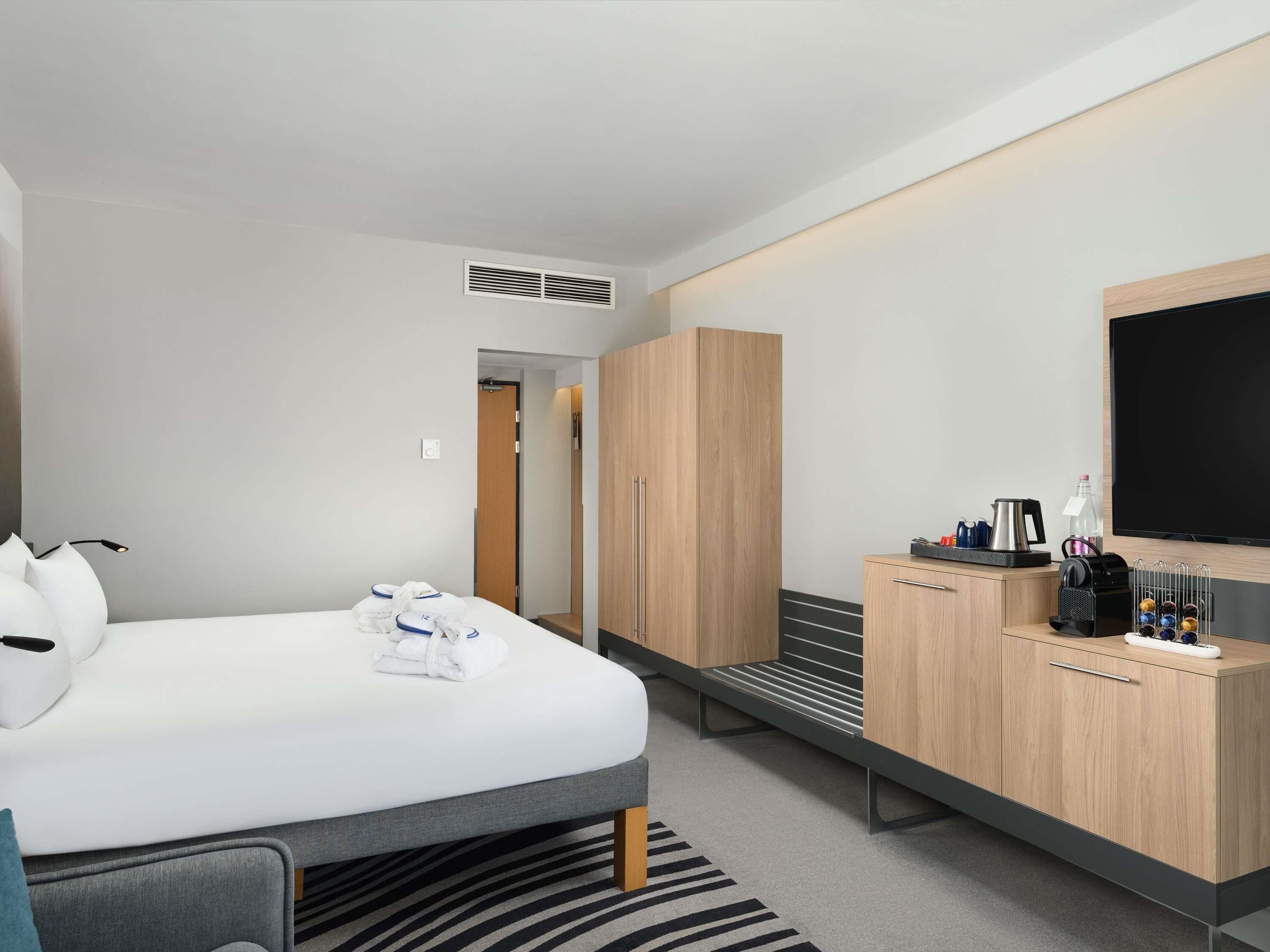 Quarto de hotel moderno com uma cama, um guarda-roupa de madeira, uma escrivaninha com uma televisão de tela plana e uma máquina de café.