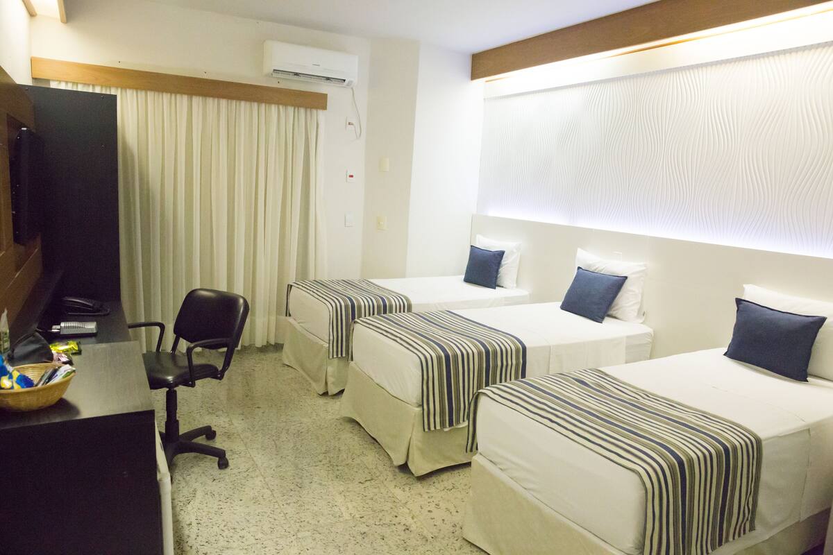 Quarto de hotel com duas camas, uma escrivaninha, uma cadeira e uma televisão.