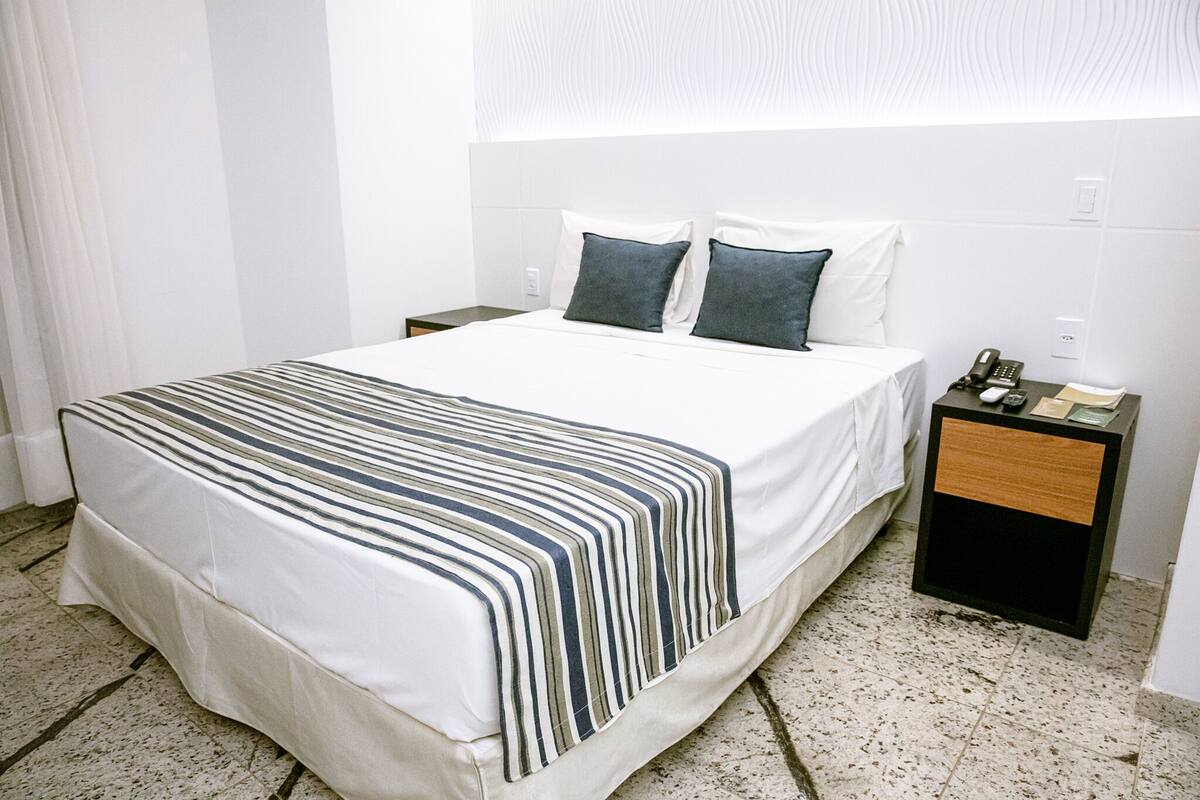 Quarto de hotel com uma cama, mesa de cabeceira e telefone.