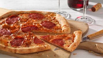 Pizza em tábua de madeira com um faca, um copo de vinho tinto e uma rolha.