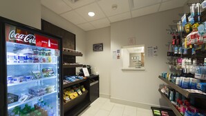 Uma área de bebidas de serviço por autoatendimento, com refrigerador de Coca-Cola, prateleiras com lanches e diversos produtos de higiene pessoal.