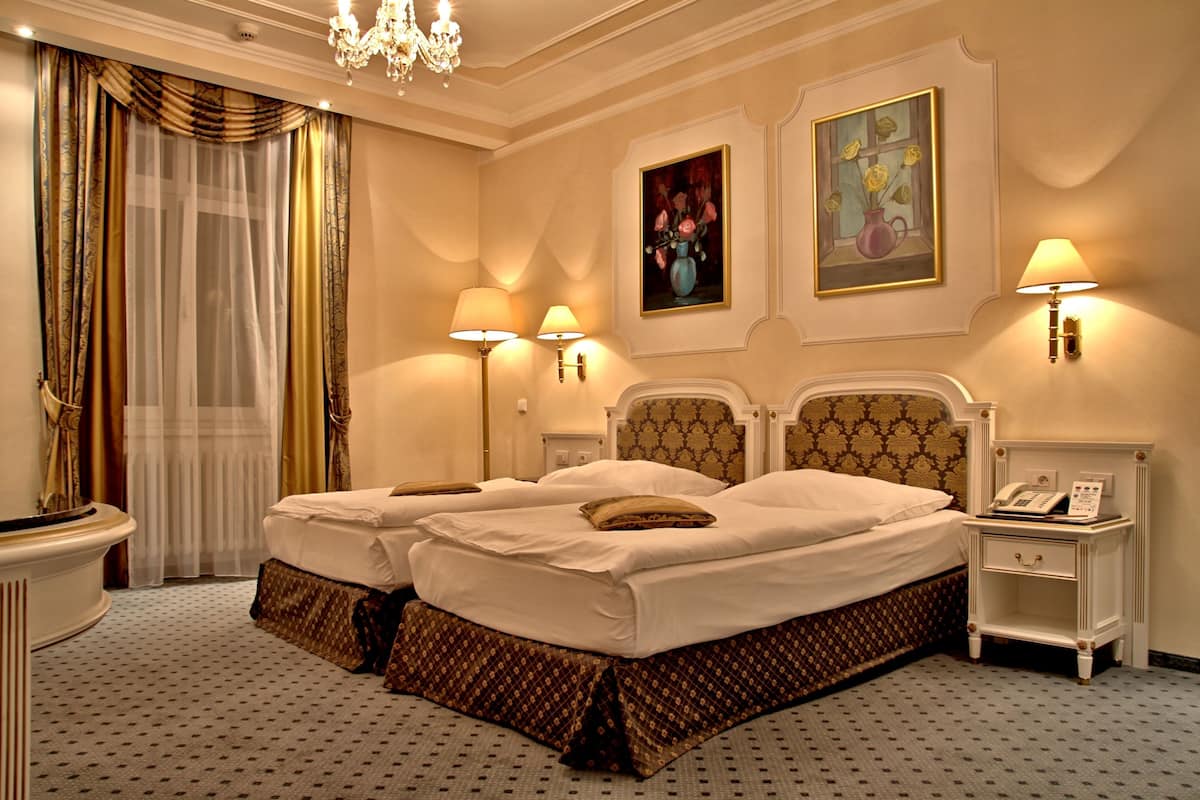 Quarto de hotel com duas camas, um candelabro, luminárias fixadas na parede e um quadro.