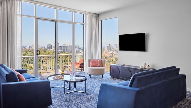 Sala de estar moderna com vista para a cidade, com sofá, poltrona e mesa de centro.