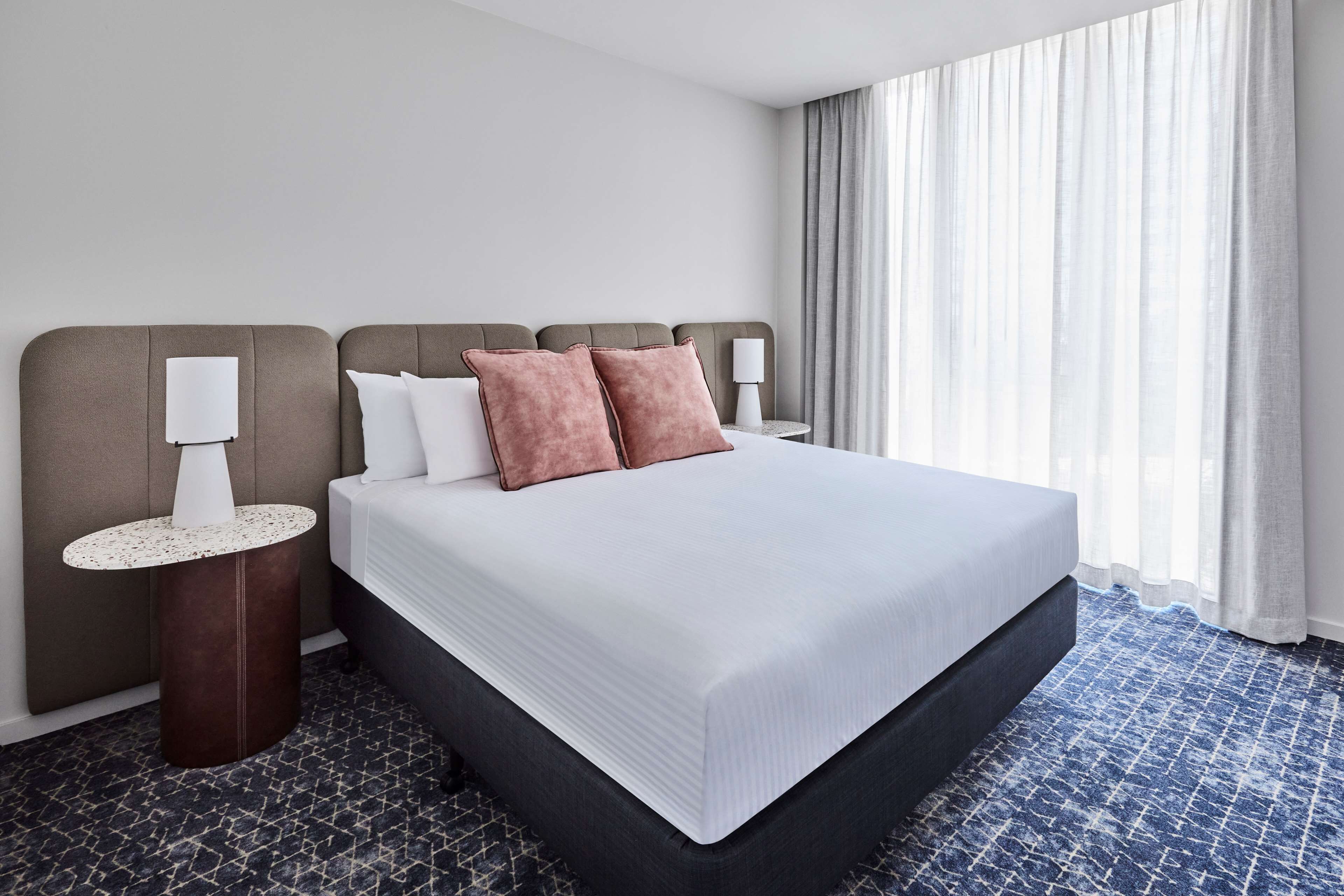 Quarto de hotel com uma cama grande, duas mesas de cabeceira e uma janela com cortinas.