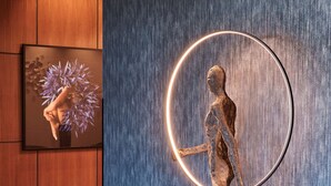 Um interior moderno com uma escultura de bronze de uma figura humana segurando um aro, em frente a uma parede azul texturizada.