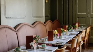 Uma área de refeições com uma mesa comprida posta para uma refeição, assentos acolchoados em camarote e uma porta com puxador de latão.