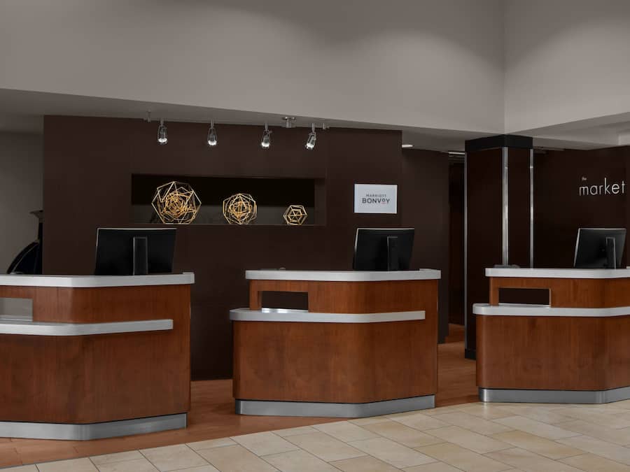 Uma área de recepção de hotel com três balcões de madeira, um aviso com 'Marriott Bonvoy' e arte geométrica na parede.