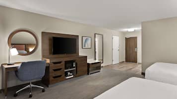 Quarto de hotel com escrivaninha, cadeira, televisão e cama.