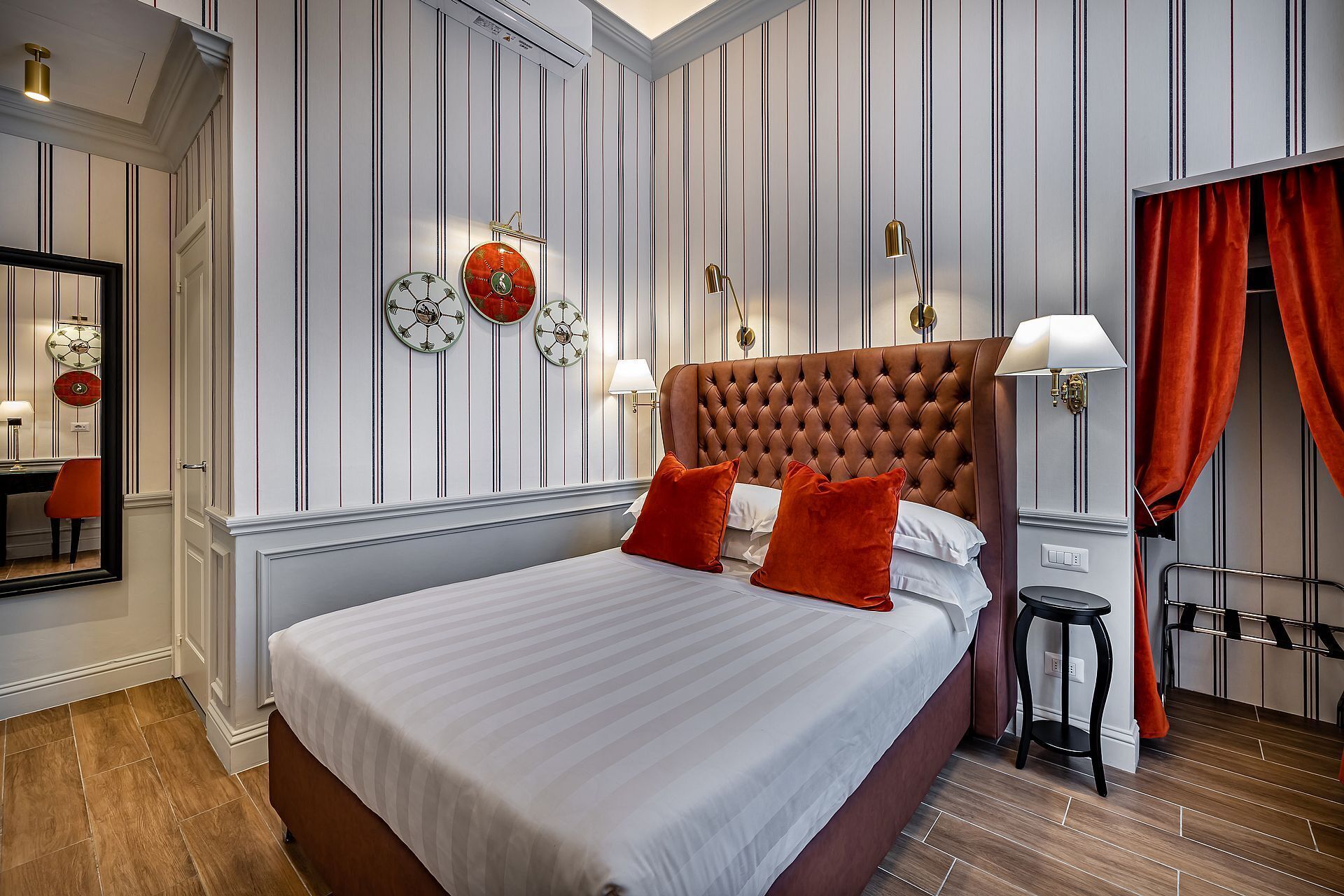 Quarto de hotel com uma cama grande, um espelho, um relógio e uma cortina vermelha.
