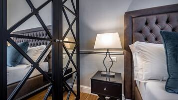 Quarto com cabeceira estofada, mesa de cabeceira com abajur e espelho com moldura geométrica.
