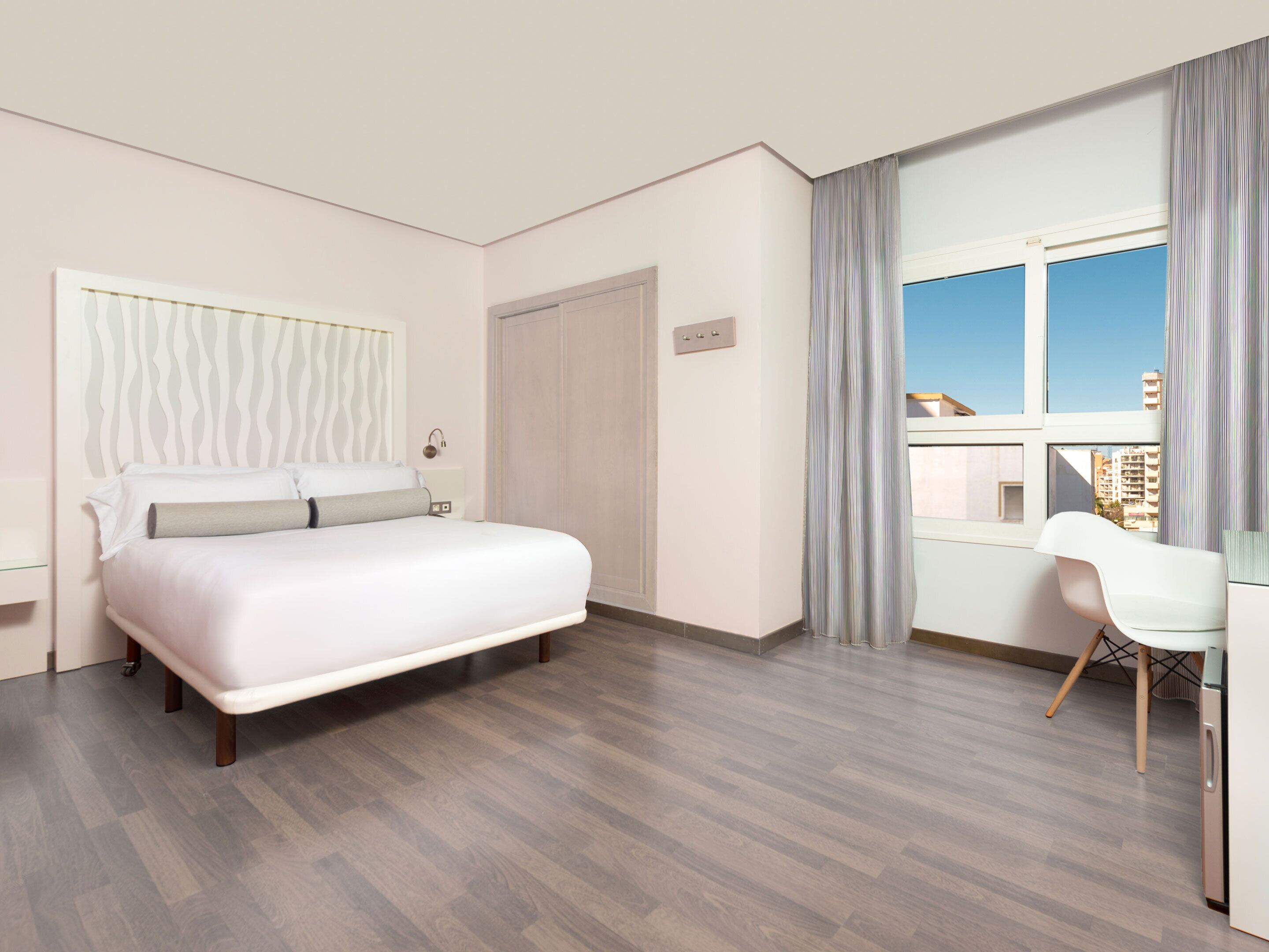 Quarto de hotel moderno com uma cama grande, uma escrivaninha e vista para a cidade.