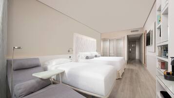 Quarto de hotel com duas camas, uma mesinha e uma luminária de cabeceira. Há um guarda-roupa e uma porta que dá para outro quarto.