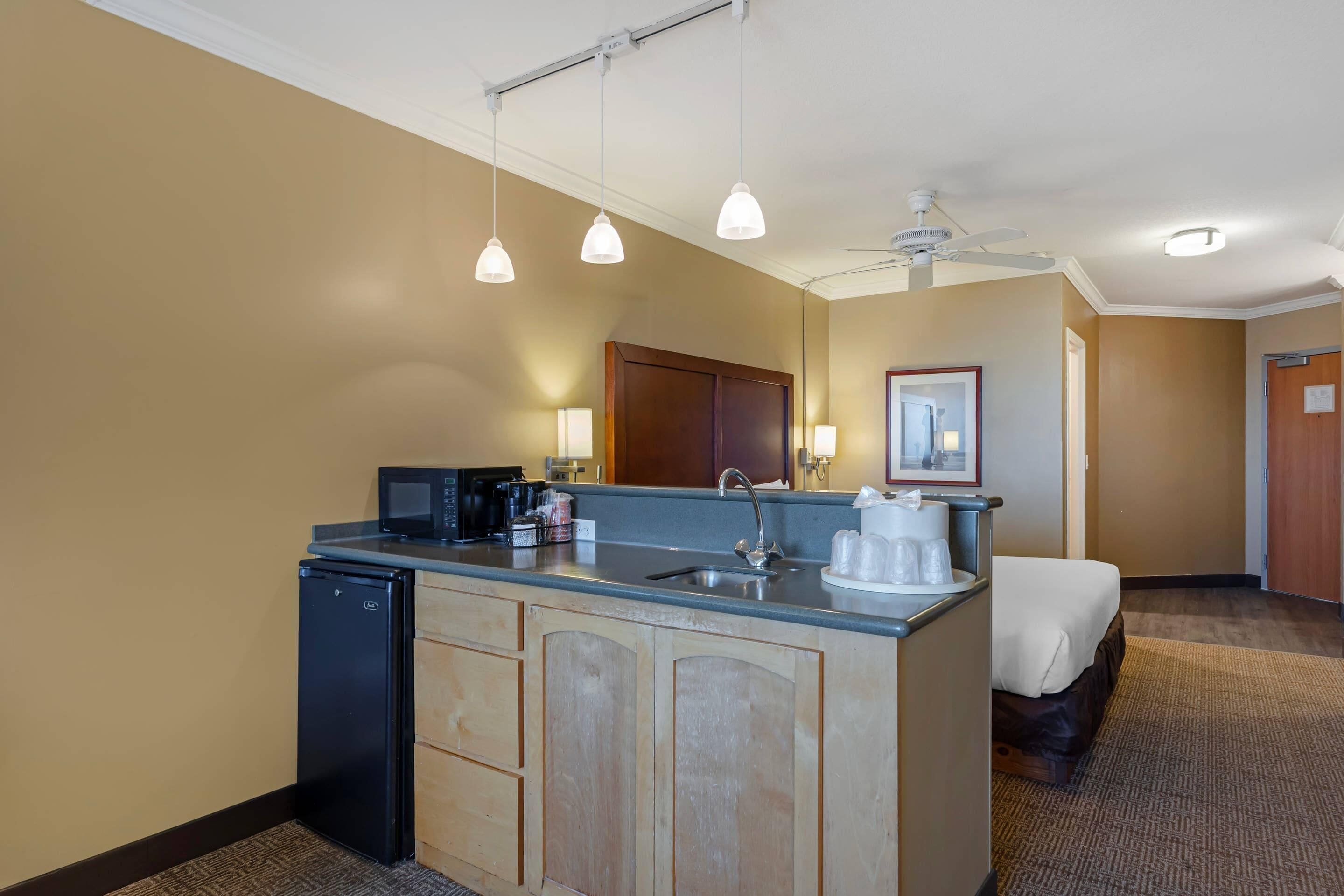 Quarto de hotel pequeno com cozinha compacta, uma cama, ventoinha no teto e banheiro modesto.