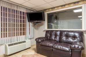 Quarto com sofá de couro, televisão na parede e janela com moldura decorativa.