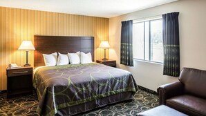 Quarto de hotel com uma cama grande, duas mesas de cabeceira com luminárias, uma poltrona de couro e uma janela com cortinas.