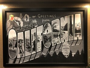 Uma placa emoldurada com a mensagem 'Greetings from California' e o prédio da capital da Califórnia ao fundo.