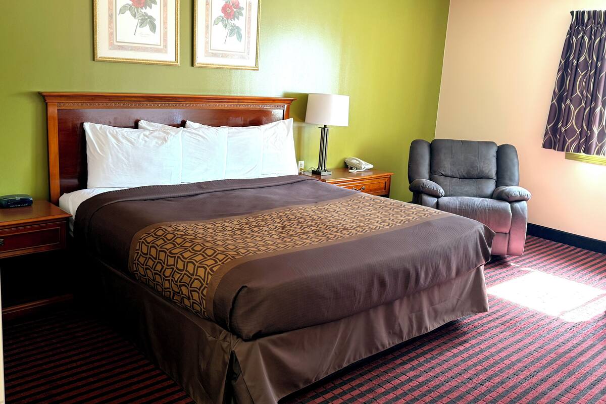Quarto de hotel com uma cama grande, mesa de cabeceira, uma cadeira e duas quadros com flores na parede.