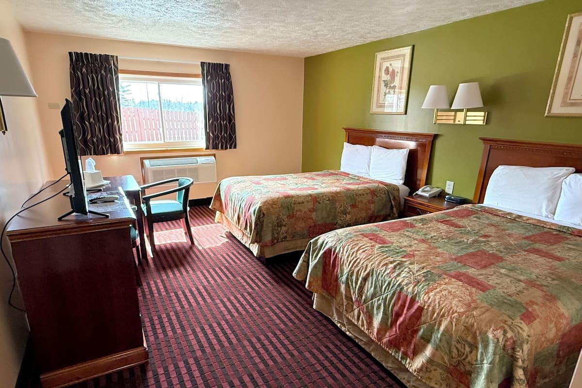 Quarto de hotel com duas camas, uma escrivaninha, uma cadeira, uma televisão e janela com cortinas.