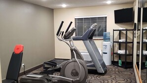 Ginásio de hotel com equipamentos de exercício, um bebedouro e uma TV na parede.
