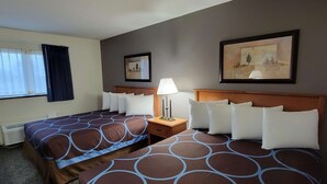 Quarto de hotel com duas camas, uma mesa de cabeceira, uma luminária e um quadro na parede.